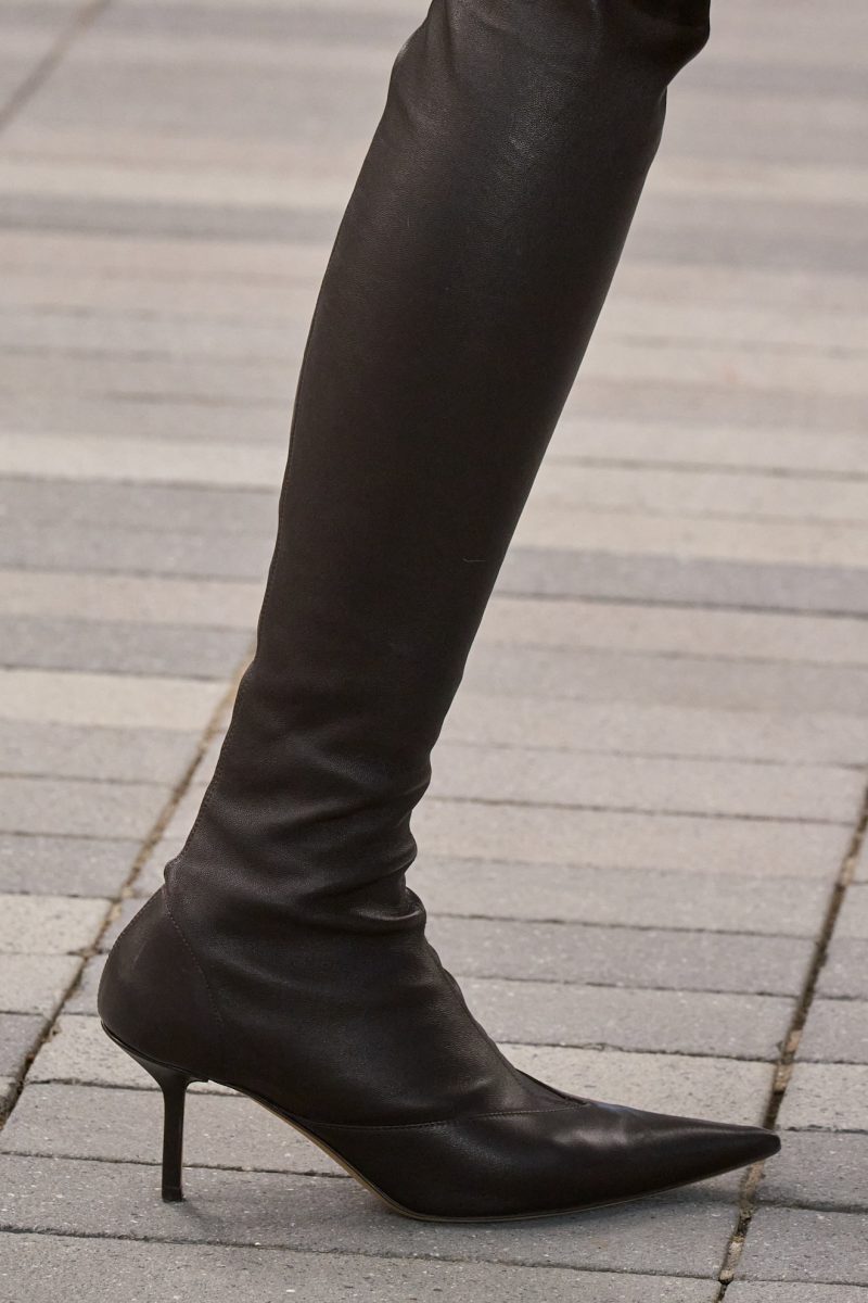 Black leather knee-high boots with pointed toe and slim kitten heel on paved sidewalk