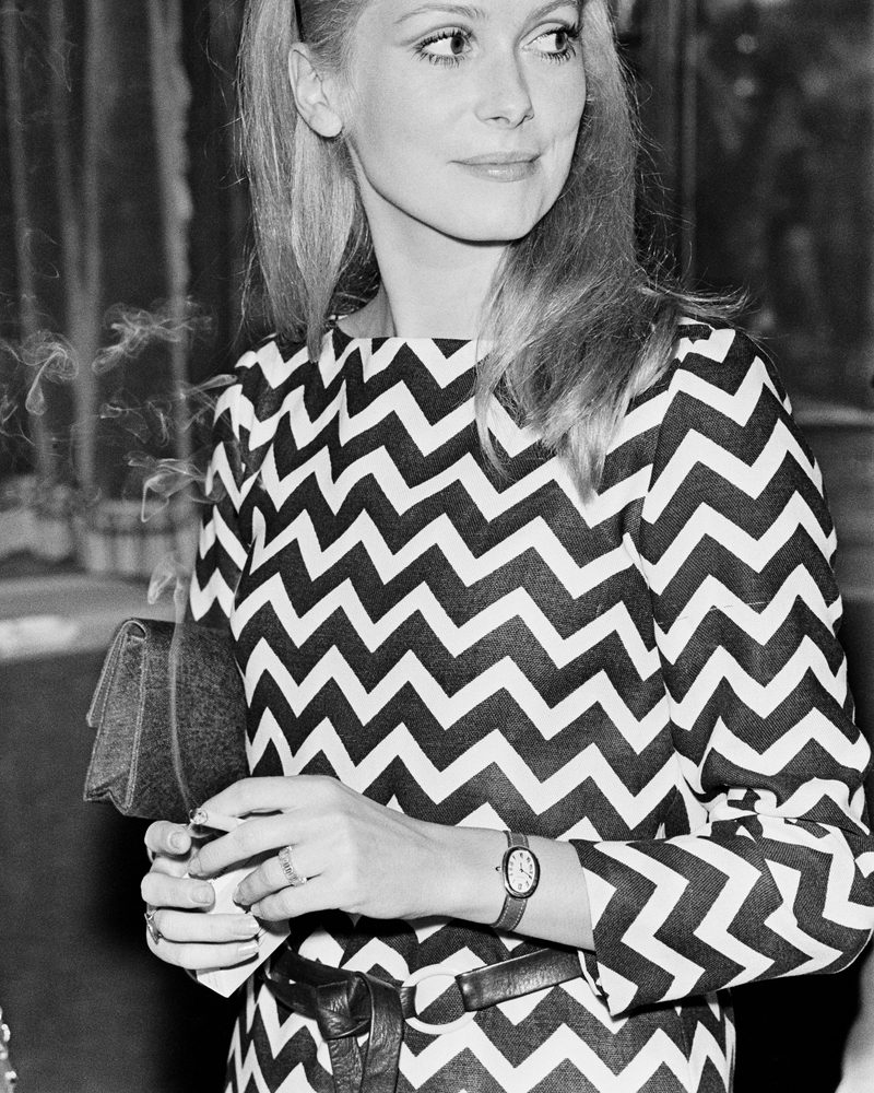 Catherine Deneuve showcases timeless elegance in a black and white chevron-patterned dress%2C complemented by vintage accessories and a sophisticated hairstyle