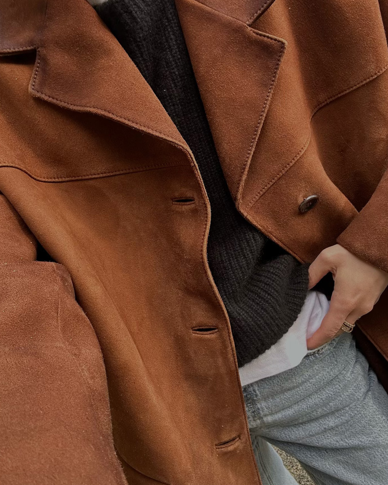 Close-up of brown suede jacket layered over a dark knit sweater and white tee with light-wash jeans
