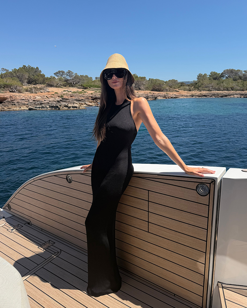 Black ribbed maxi dress styled with a woven bucket hat and oversized sunglasses aboard a yacht on a sunny coastal day