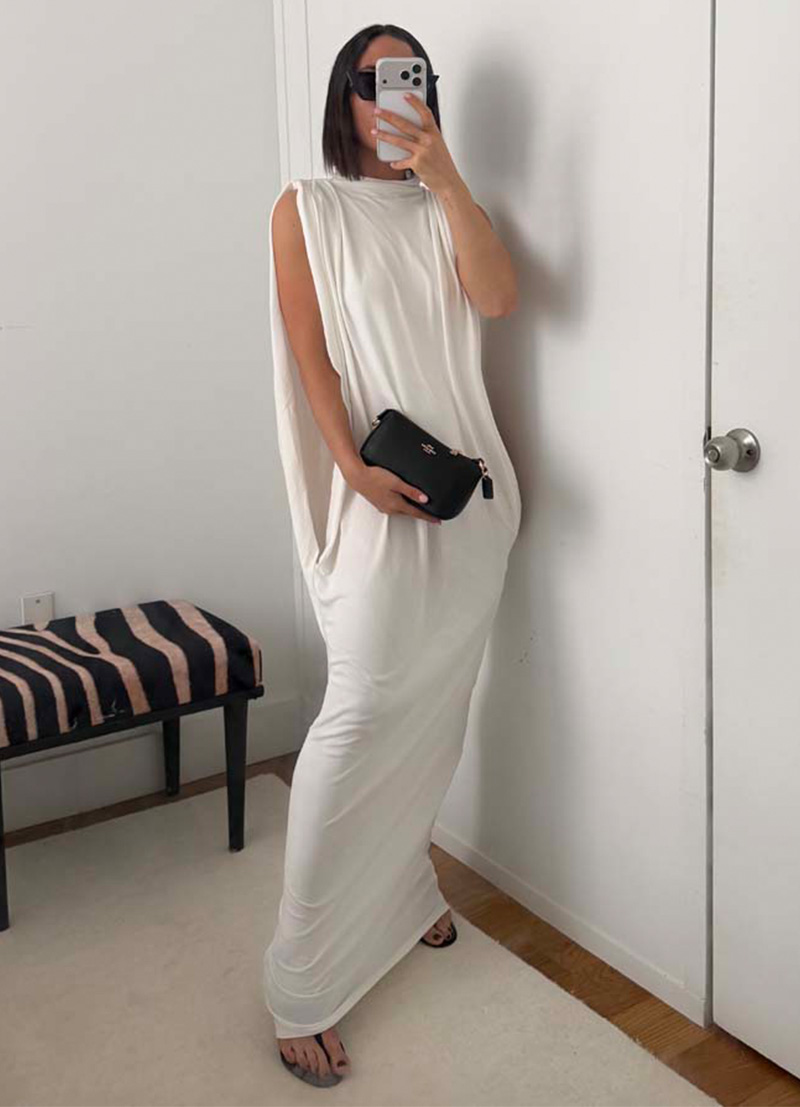 Mirror selfie in a white draped maxi dress with black clutch and flat sandals in a minimalist room