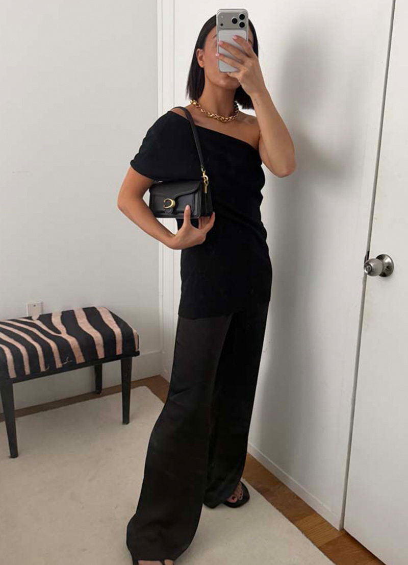 Mirror selfie in a black off-shoulder top, wide-leg trousers, gold necklace and shoulder bag in a minimalist room