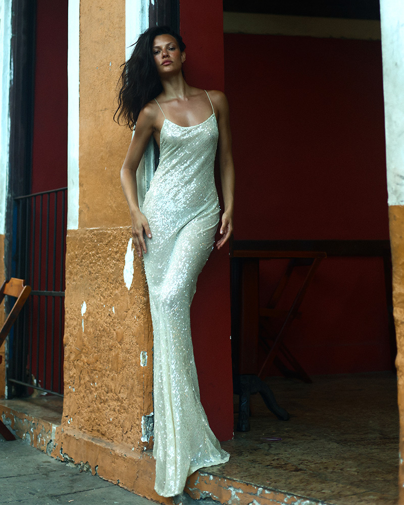 Sparkling white sequin slip gown with delicate straps%2C styled in a rustic doorway for an elegant evening look%0A
