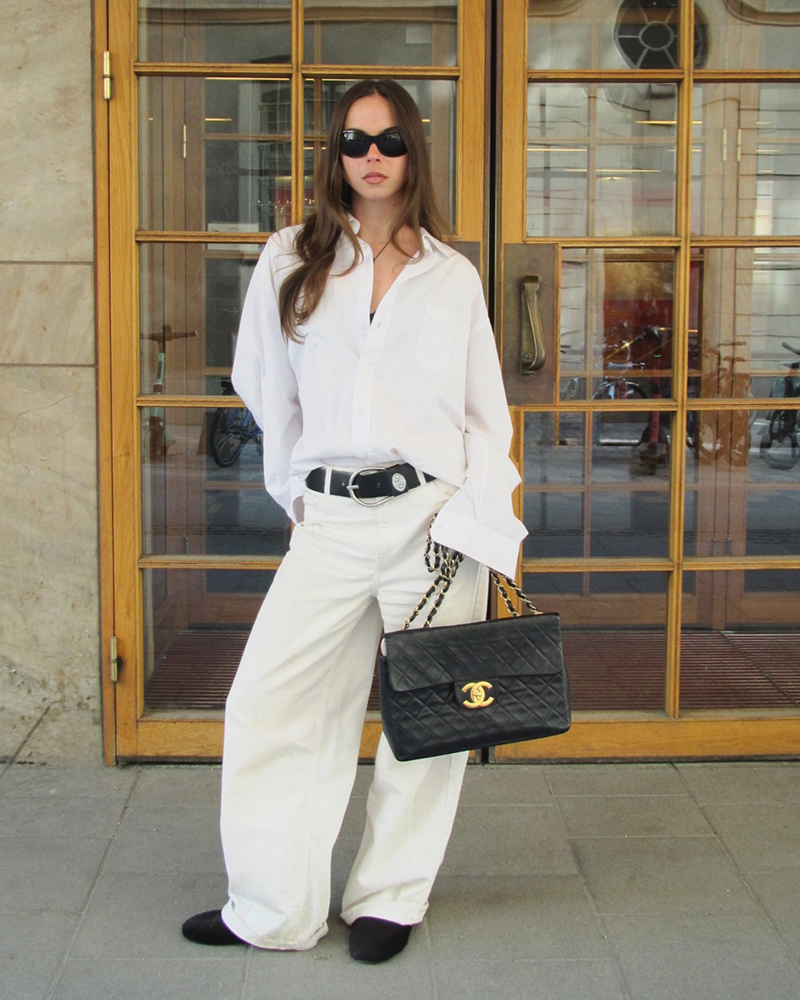 White shirt and wide-leg trousers styled with sunglasses and a black Chanel quilted bag outside glass doors