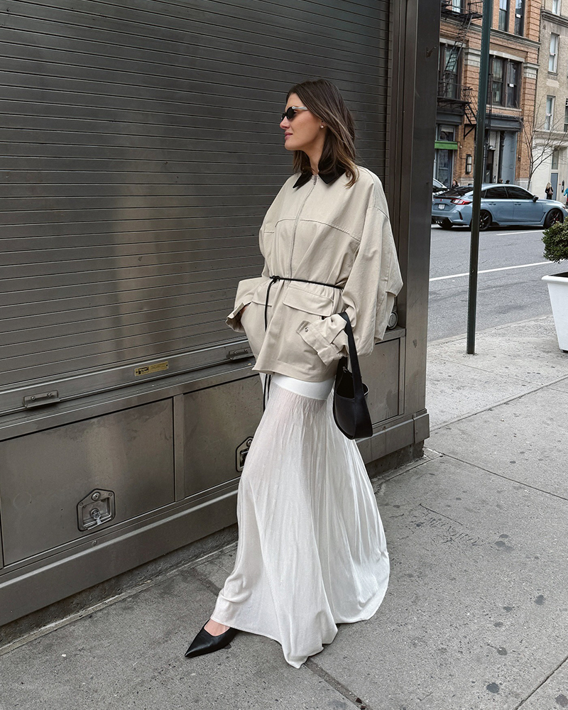 Cream utility jacket and flowing white maxi skirt styled with black accessories on a city sidewalk