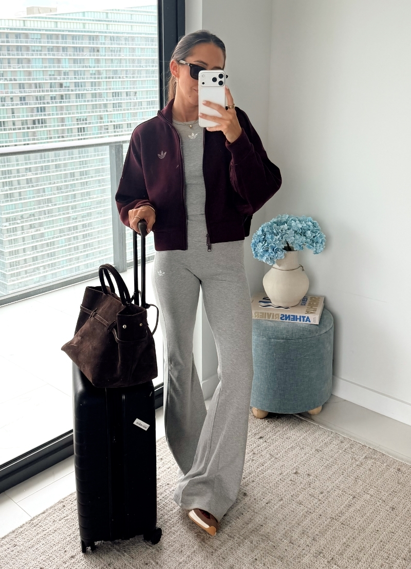 Model in a burgundy jacket, cream jeans and retro sneakers with a shoulder bag in a bright apartment