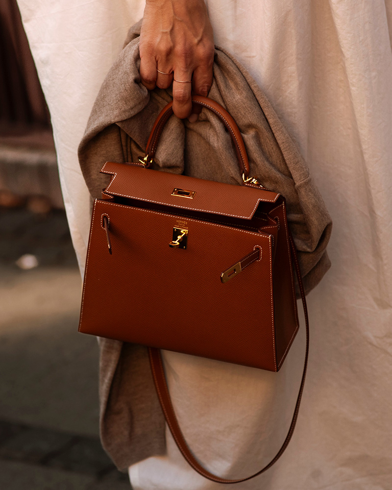 Herm%C3%A8s Kelly brown leather handbag with gold-tone hardware%2C styled with a cream dress on a Copenhagen street%0A