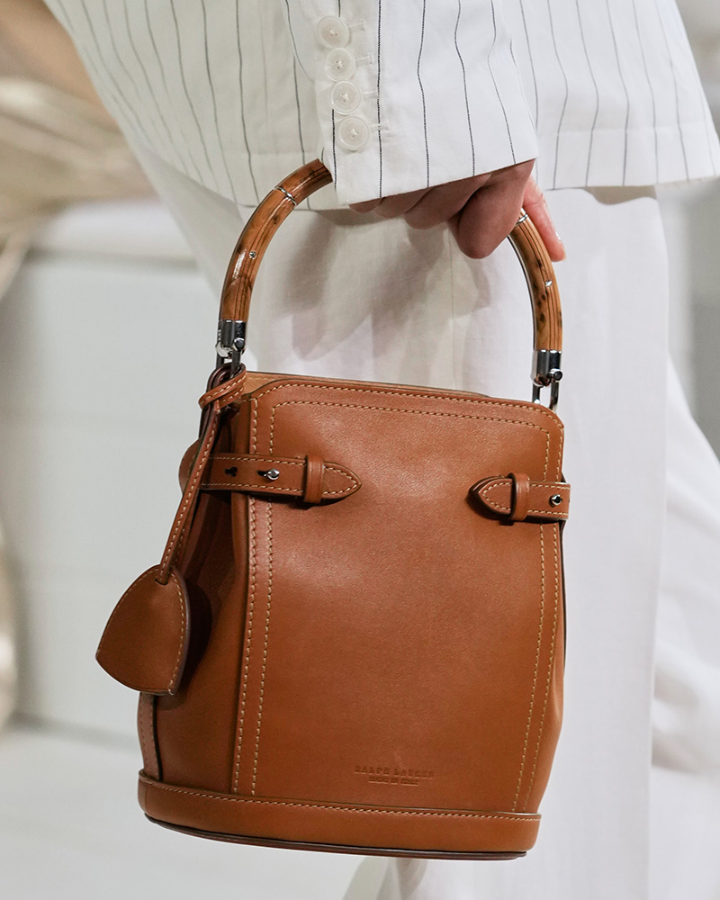 Ralph Lauren brown leather bucket bag with bamboo top handle%2C styled against a crisp white tailored suit%0A
