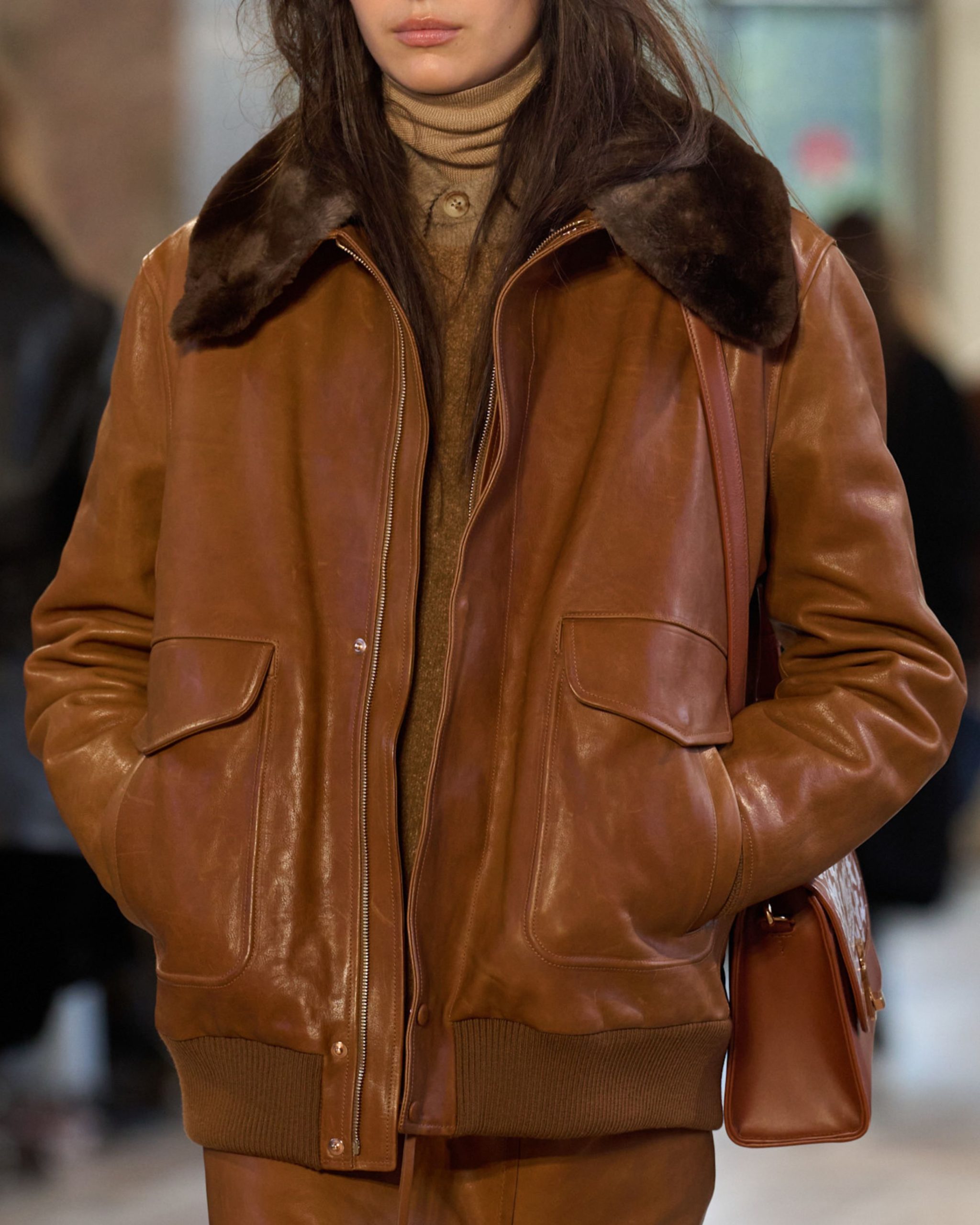 Brown leather bomber jacket with dark fur collar%2C paired with tan turtleneck and matching leather bag for fall fashion