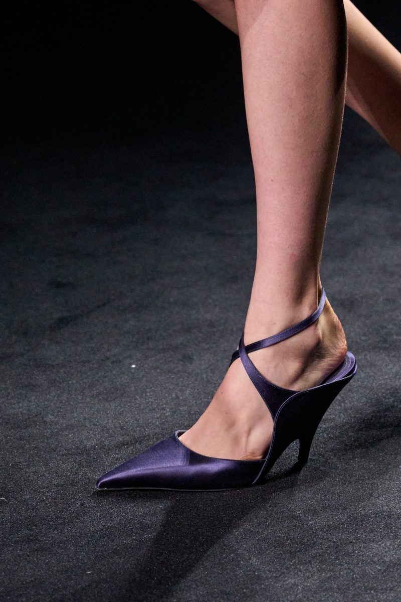 Purple satin pointed-toe slingback heels with crisscross ankle straps on runway model's foot