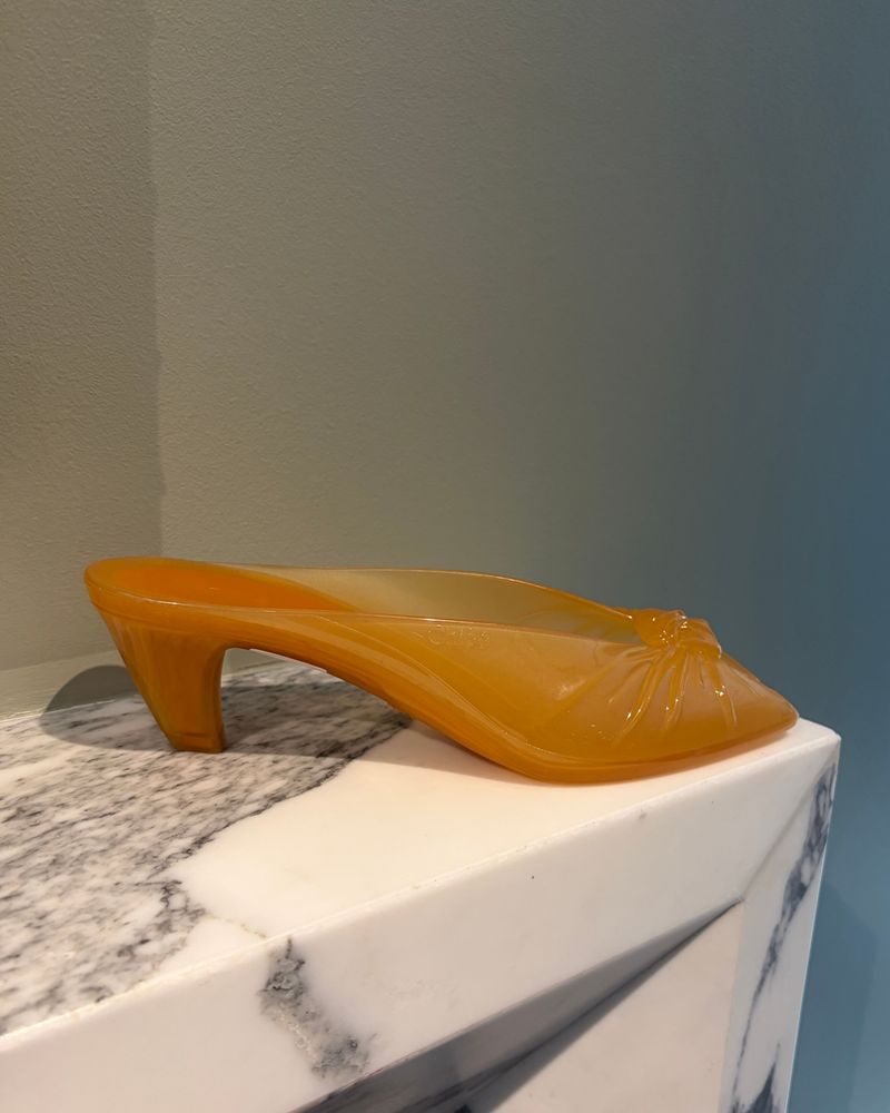 Yellow jelly mule with low block heel and ruched toe detail on marble surface