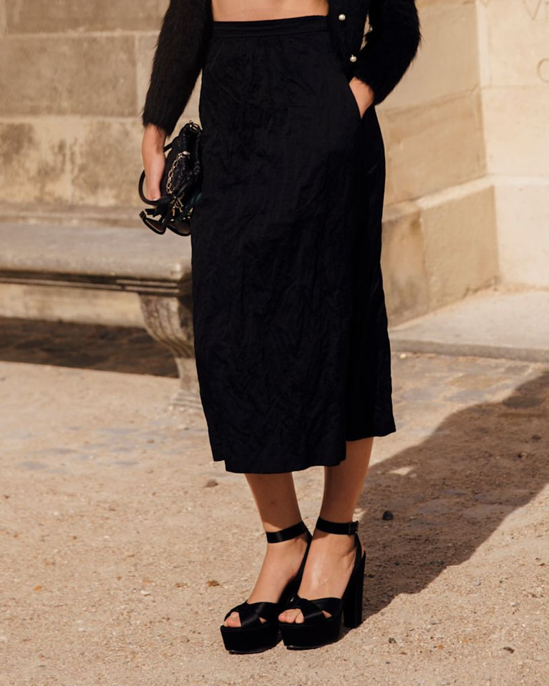 Model wearing a black bandeau top%2C fuzzy cropped cardigan%2C high-waisted midi skirt%2C and platform heels in a Paris street style setting