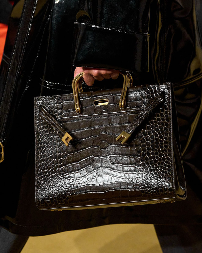 Tory Burch black crocodile embossed leather handbag with gold hardware and structured top handles held with glossy black coat sleeve