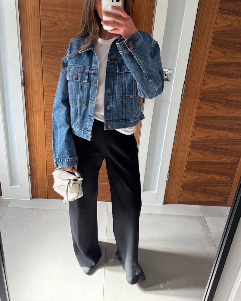 Chic outfit featuring a cropped denim jacket over a white tee%2C paired with black wide-leg pants and a stylish beige clutch.