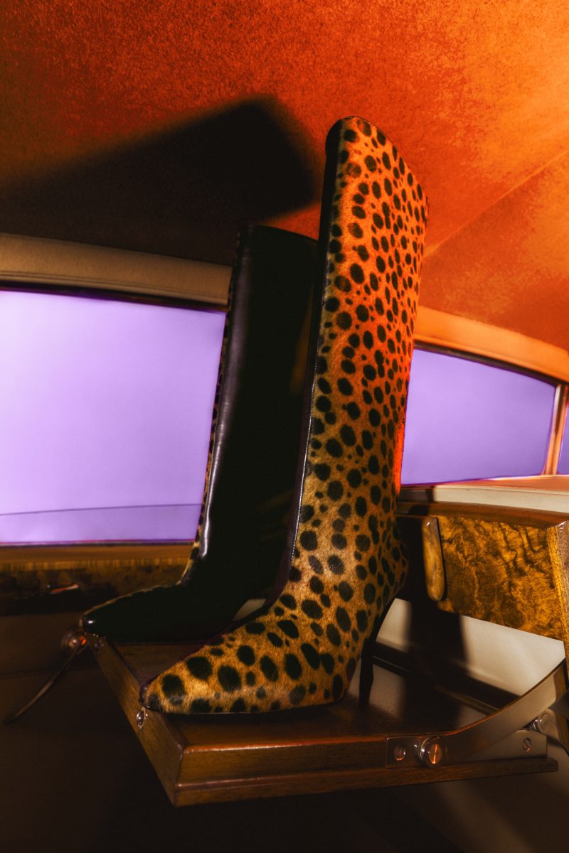 Knee-high leopard print boots with pointed toes and stiletto heels displayed inside a vintage car interior