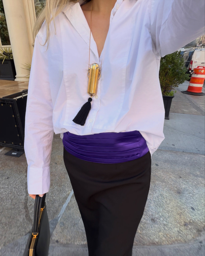 Chic outfit featuring a crisp white button-up shirt%2C a bold purple cummerbund%2C and a sleek black skirt%2C accessorized with a gold tassel necklace