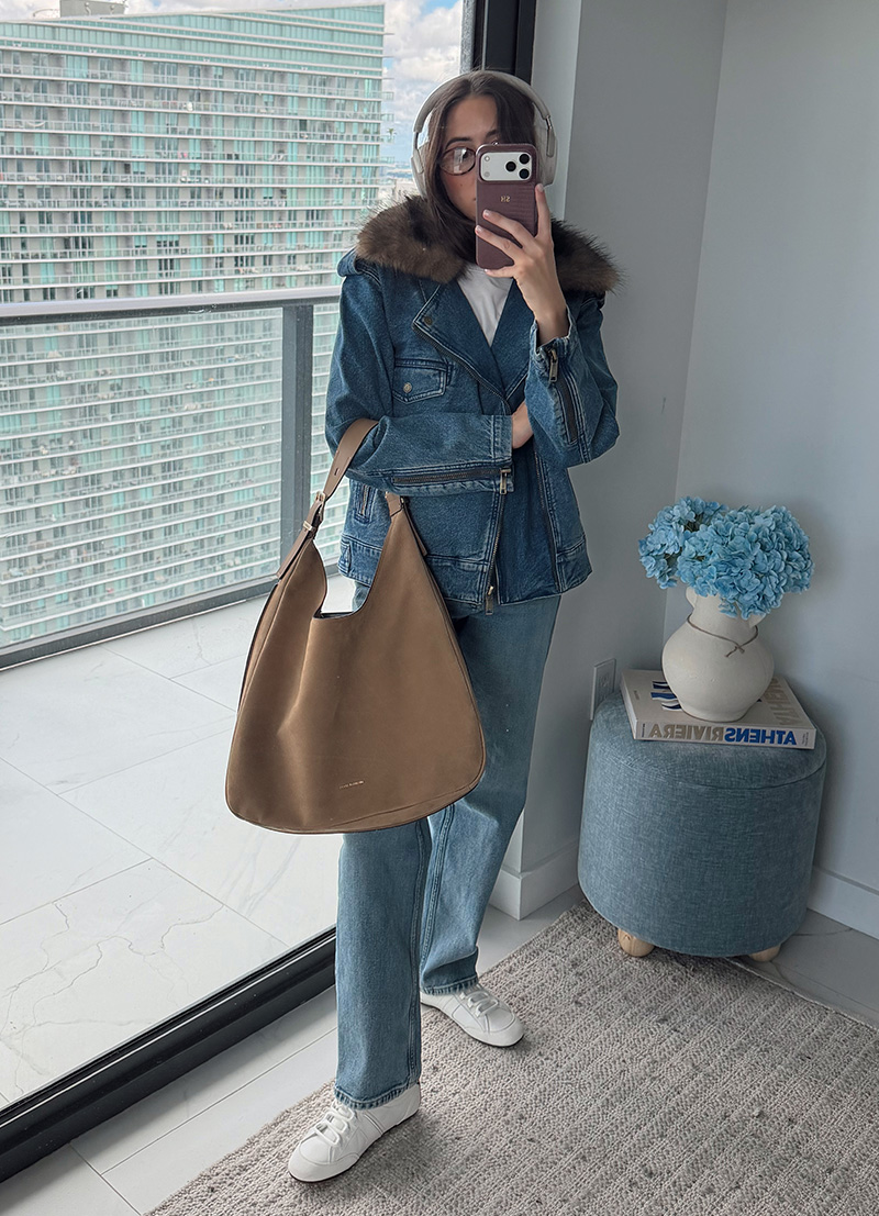 Blue denim jacket with faux-fur collar styled with wide-leg jeans, white sneakers, and a tan hobo bag indoors