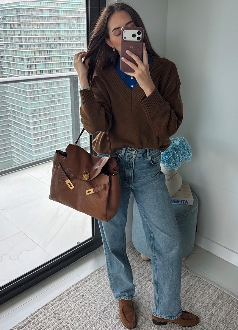 Brown V-neck sweater over a blue polo styled with relaxed jeans, suede loafers, and a brown leather handbag