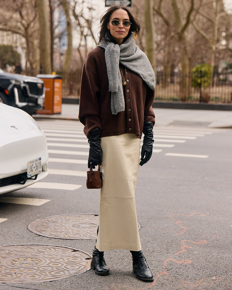 Brown cardigan styled with a gray scarf%2C cream maxi skirt%2C black leather gloves and boots on a city street