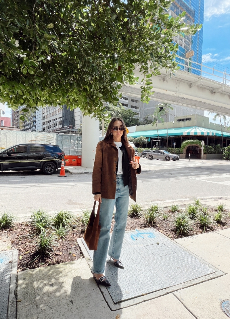 Brown suede jacket paired with light-wash jeans, pointed flats and matching tote on a sunny city sidewalk