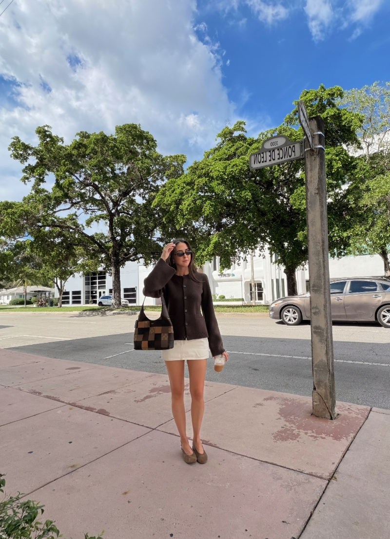 Brown cardigan paired with white shorts, ballet flats and a patchwork shoulder bag on a sunny city street
