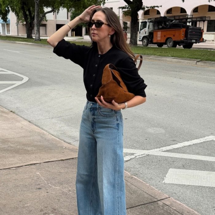 Black cardigan paired with wide-leg jeans, pointed flats and a brown suede bag on a tree-lined city street