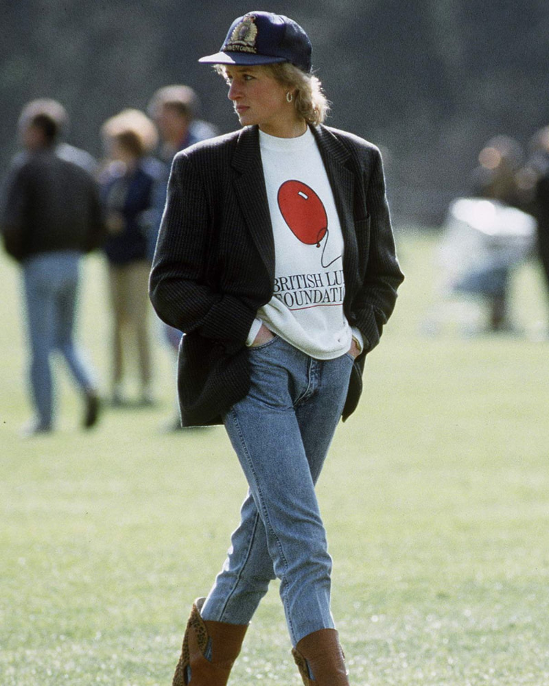 Woman wearing a British Lung Foundation white graphic sweatshirt%2C oversized pinstripe blazer%2C light wash jeans%2C brown leather cowboy boots%2C and a navy baseball cap