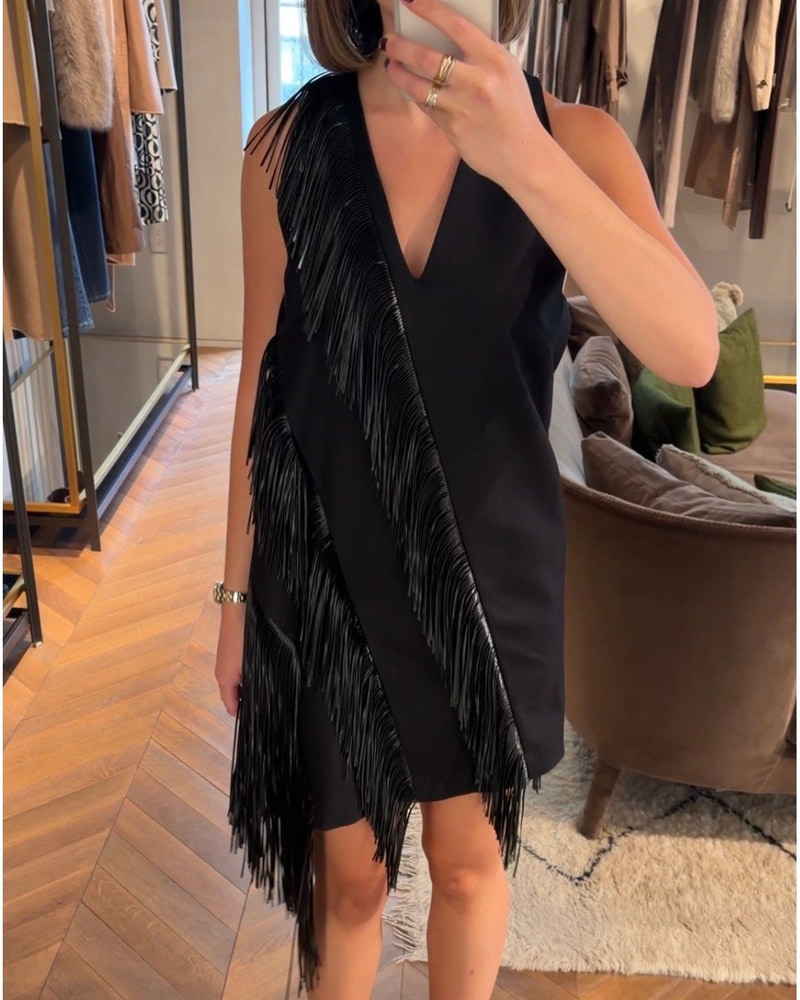 Black sleeveless mini dress with asymmetrical fringe detailing paired with black pointed-toe heels in a boutique setting