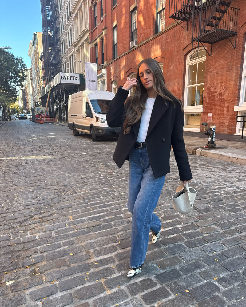 Chic fall outfit featuring a tailored black blazer over a white top%2C paired with light denim flared jeans and trendy printed ankle boots%2C complemented by a sleek silver handbag.