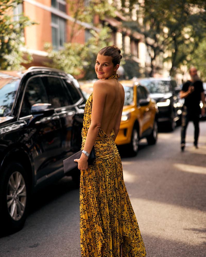 Flowy yellow maxi dress with a floral print and open back%2C paired with a chic black clutch and strappy heels%2C captured on a vibrant New York street
