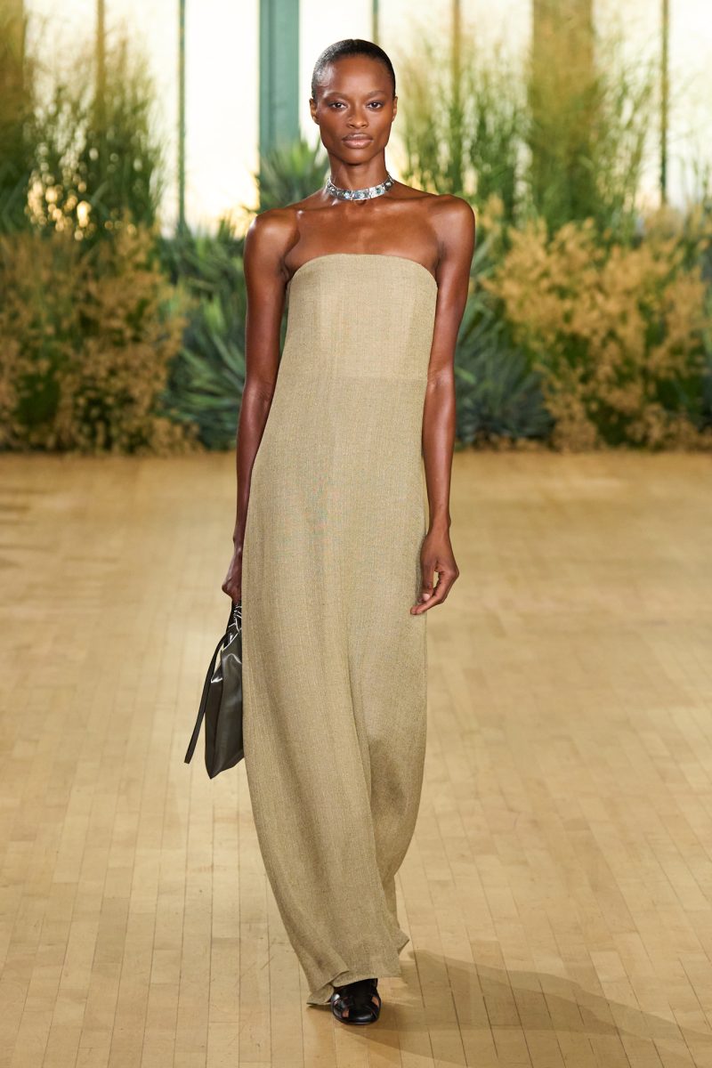 Model wearing a strapless beige linen maxi dress with a silver choker necklace and black handbag on runway