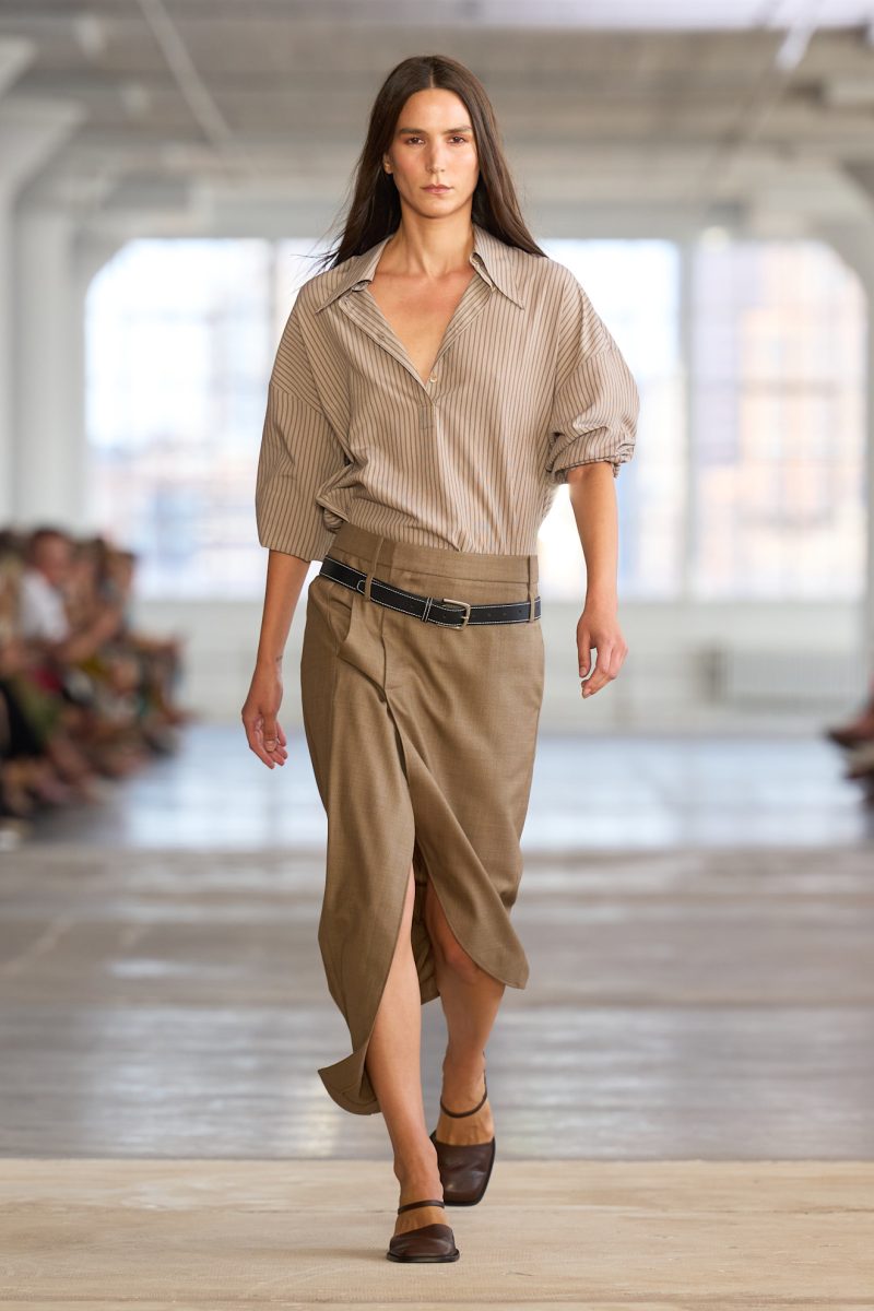Model wearing a beige pinstripe oversized shirt paired with a high-waisted brown midi skirt with front slit and black belt, styled with brown leather flats