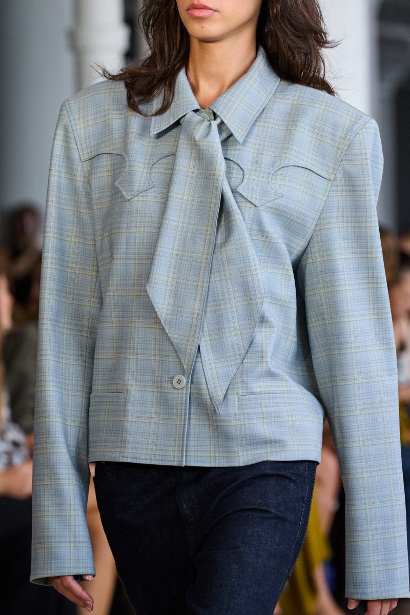 Light blue plaid blazer with oversized bow tie collar and structured shoulders paired with dark denim jeans on runway