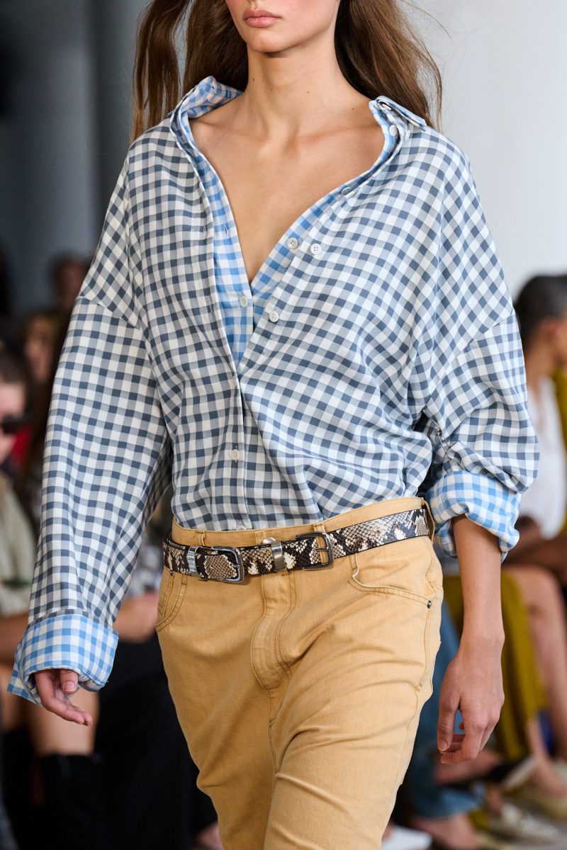 Model wearing oversized blue and white gingham check shirt with rolled cuffs paired with camel-colored pants and a snakeskin belt