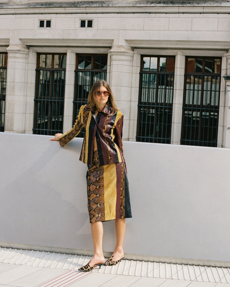 Stylish model wearing a multicolored shirt dress with snake print and bold stripes%2C complemented by chic leopard print flats and oversized sunglasses