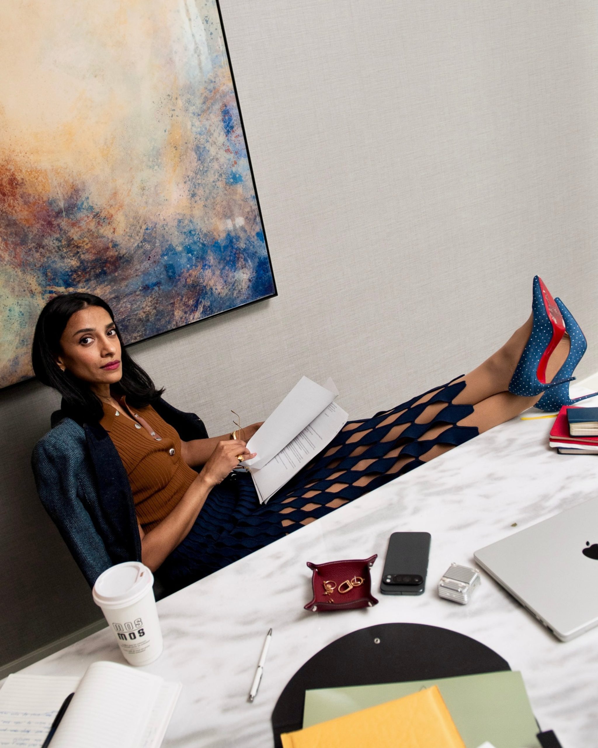 Woman wearing a brown ribbed top with a navy blue cutout skirt and blue polka dot Christian Louboutin heels in a modern office setting