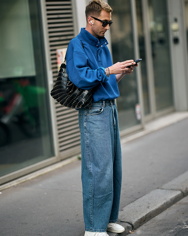 Blue pullover styled with wide-leg jeans%2C white sneakers and a black woven shoulder bag on a city street
