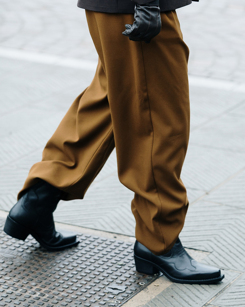 1. Black Western boots paired with relaxed brown trousers and leather gloves while walking along a city sidewalk
