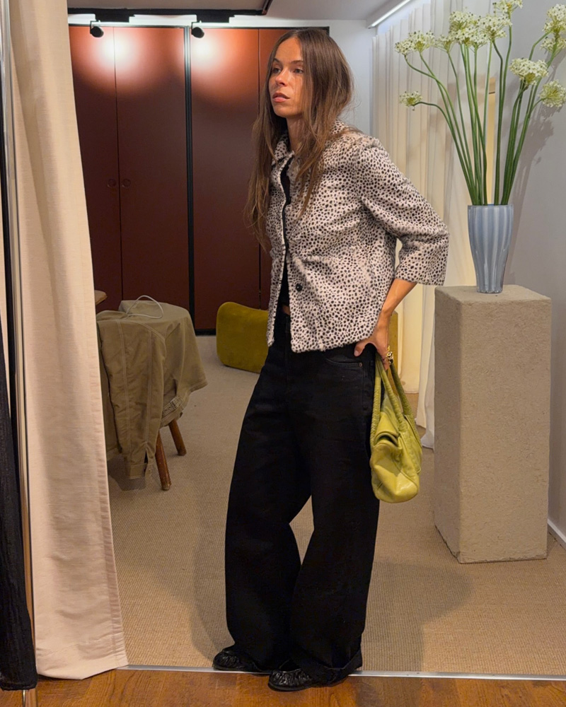 Spotted animal-print jacket styled with black wide-leg trousers%2C dark flats and a lime green handbag in a minimalist interior