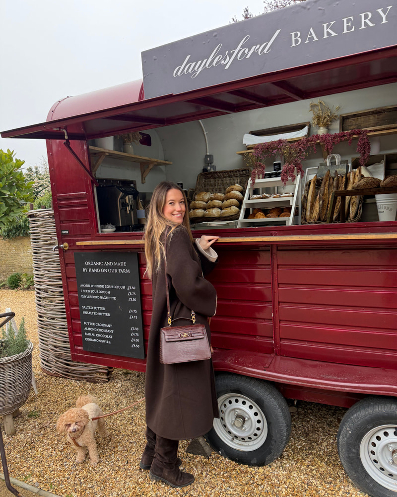 Chic autumn outfit featuring a long brown coat paired with cozy brown knee-high boots%2C accessorized with a stylish crossbody bag at a charming bakery